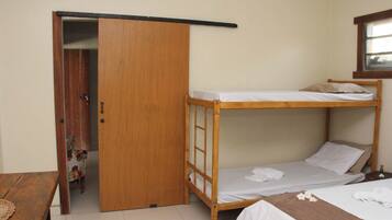 Quarto individual com uma cama beliche de madeira, porta que dá para outro quarto e uma pequena mesa com um tapete de fibra natural.