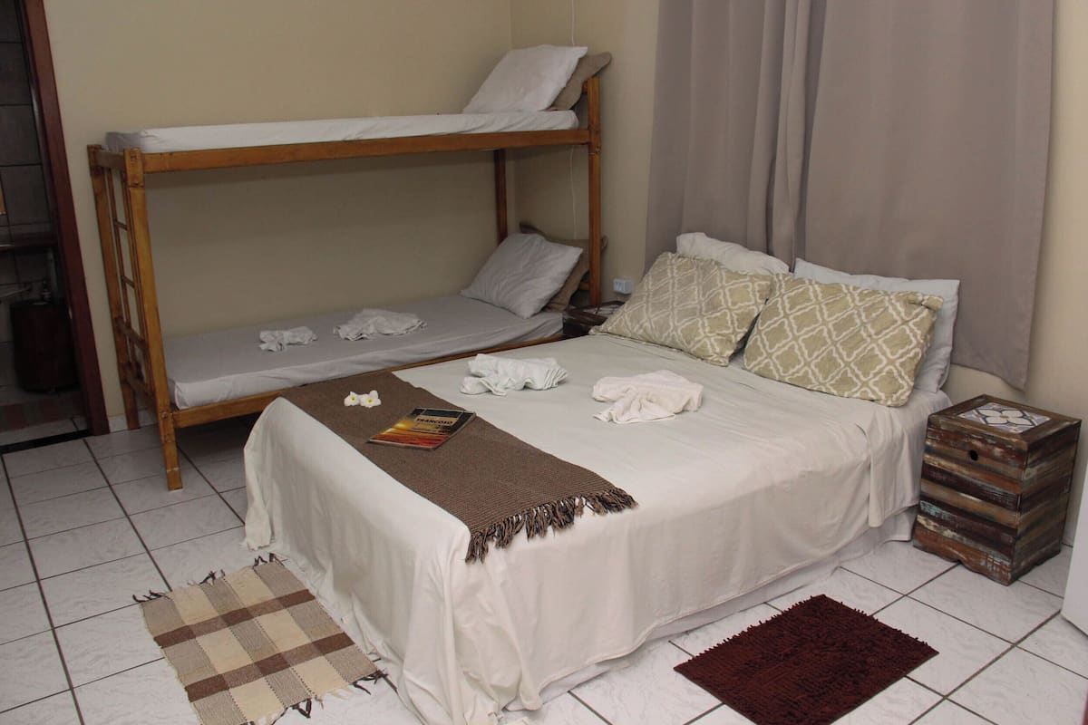 Quarto com beliche, edredom branco, almofadas, cobertor e uma pequena mesa de cabeceira de madeira.