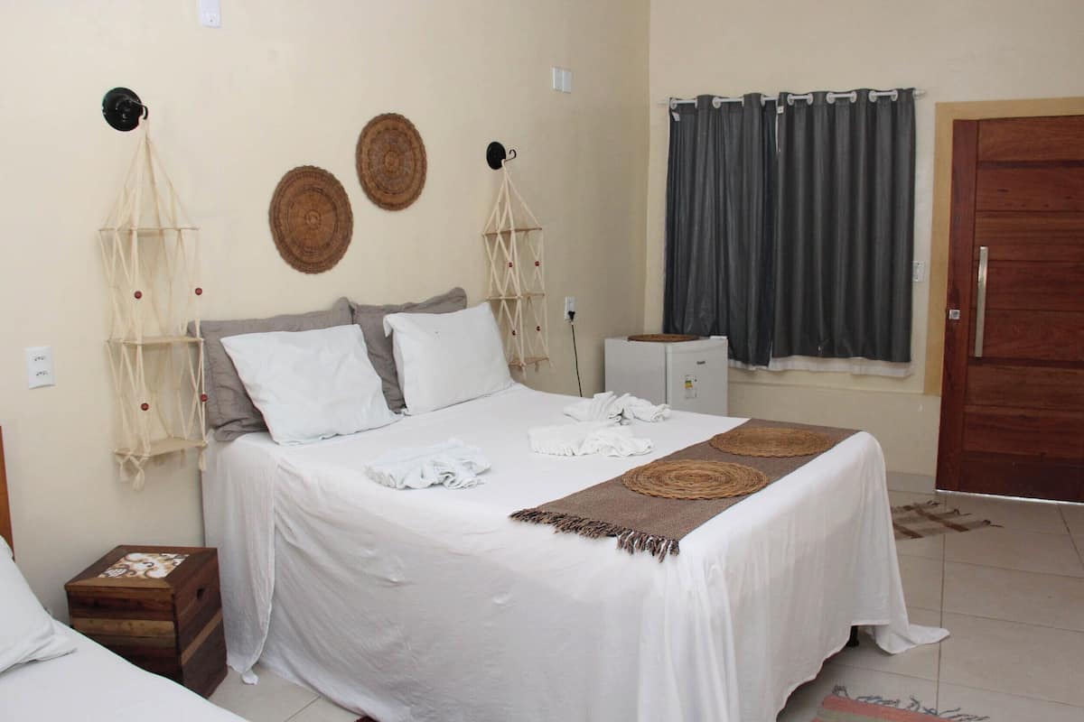 Um quarto com cama, mesas de cabeceira, guarda-roupa e janela com cortinas.
