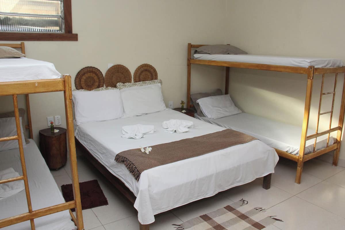 Quarto com duas beliches, uma cama de solteiro e uma mesa redonda pequena.