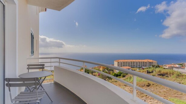 Varanda com mesa e cadeiras, com vista para a costa e edifícios ao longe.