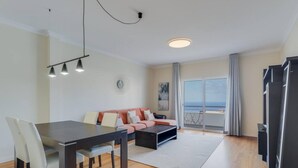 Uma sala de estar moderna com uma mesa de jantar, sofá e uma janela grande com vista para o mar.