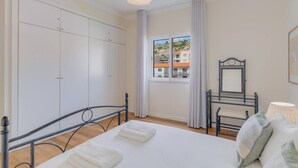Quarto com cama, guarda-roupa, espelho e janela com vista para prédios.