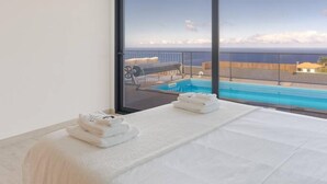 Quarto de hotel com uma grande janela que oferece vista para uma piscina e o mar.