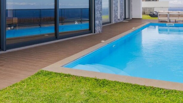 Um edifício moderno com piscina, janelas amplas e vista para o mar.