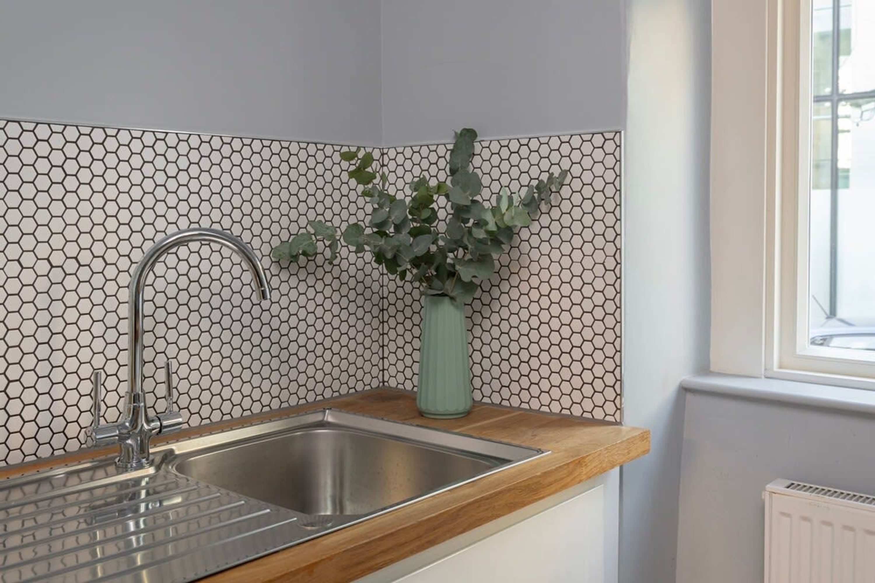 Cozinha com pia de aço inoxidável, bancada de madeira e painel de fundo com padrão hexagonal.