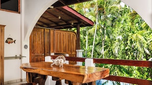 Uma mesa de jantar de madeira com bancos, um armário de madeira e vista para vegetação exuberante.