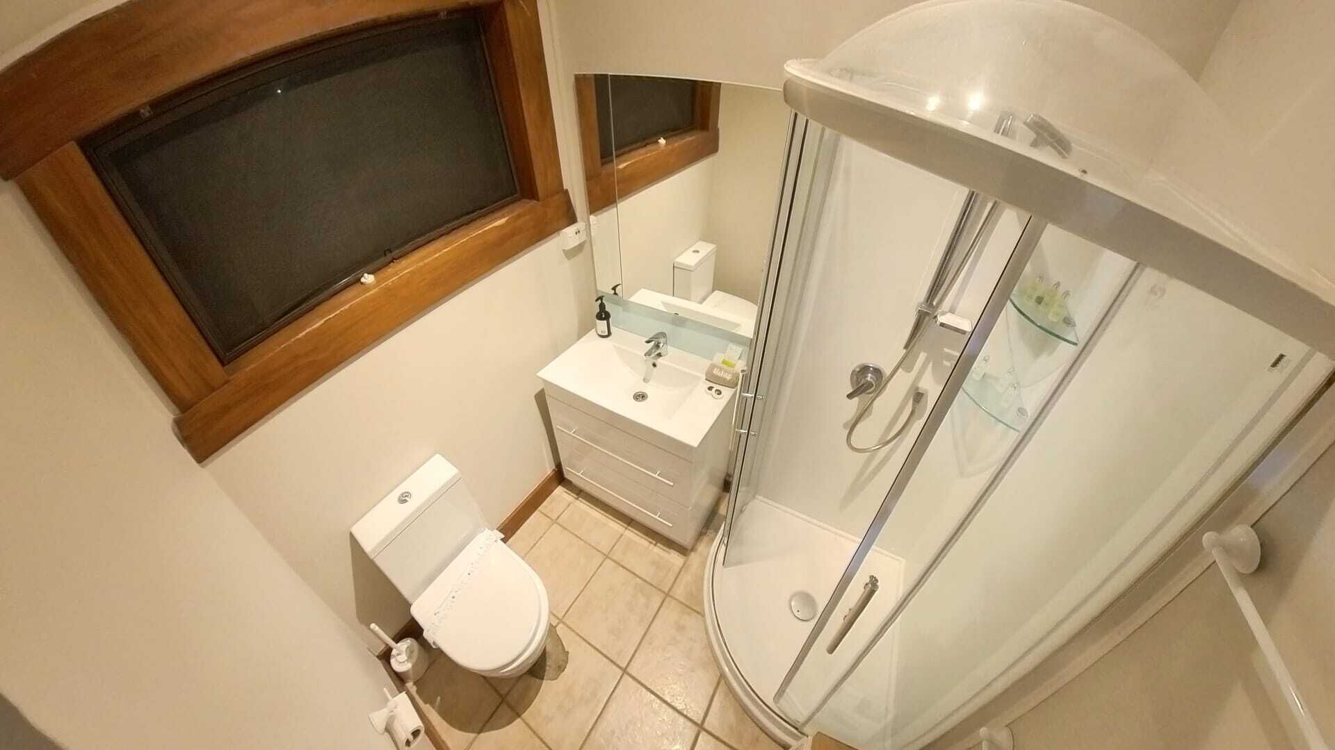 Casa de banho compacta com sanita, lavatório e chuveiro.
