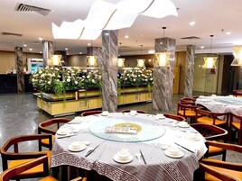 Restaurante com mesas redondas preparadas para refeições, um arranjo floral central e pilares de mármore.