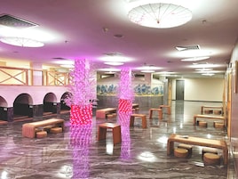Um hall com áreas de estar, balcão de recepção e elementos decorativos, como flores cor-de-rosa iluminadas.