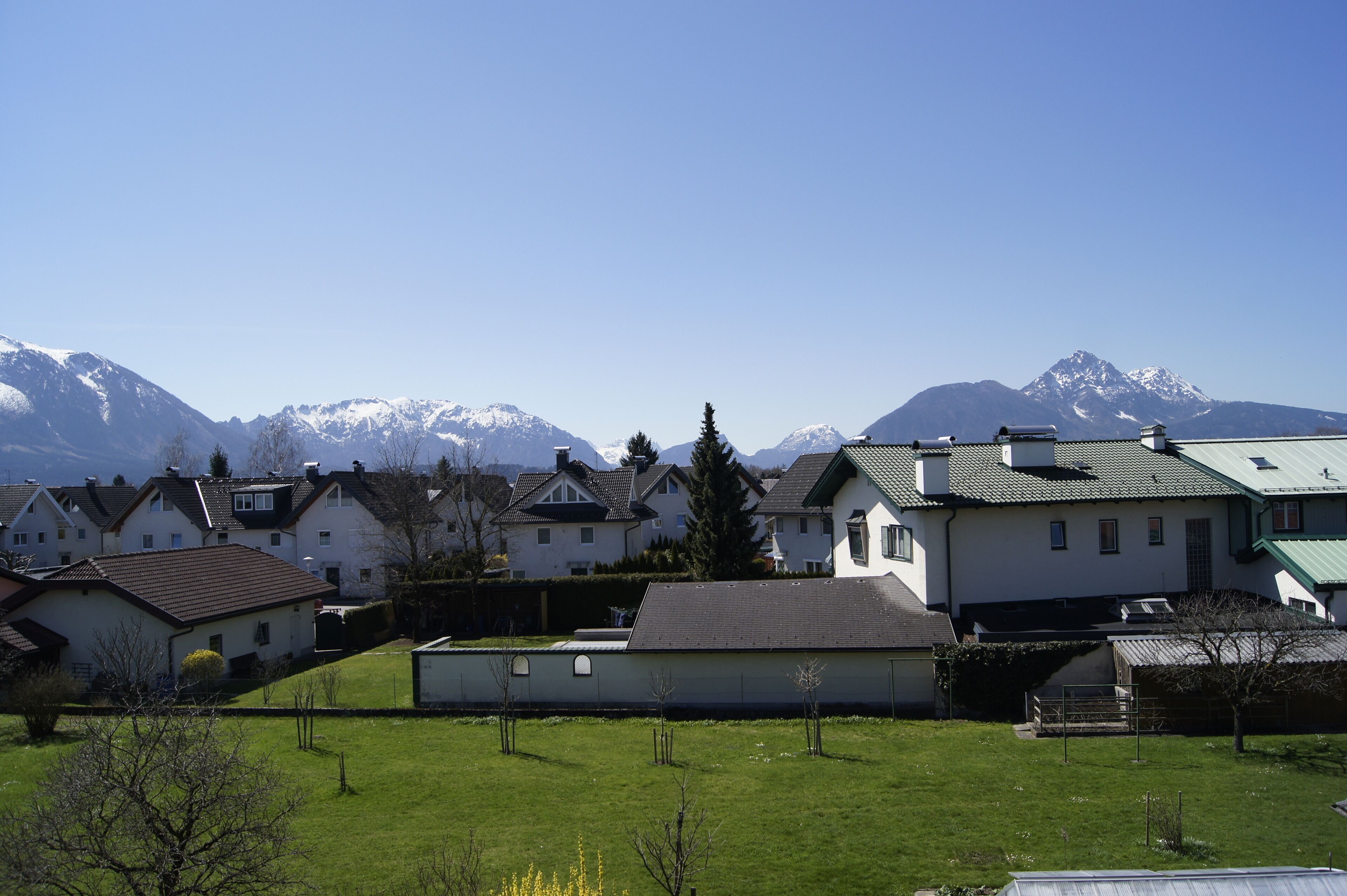 Um bairro residencial com casas, um gramado verde e montanhas nevadas ao fundo.
