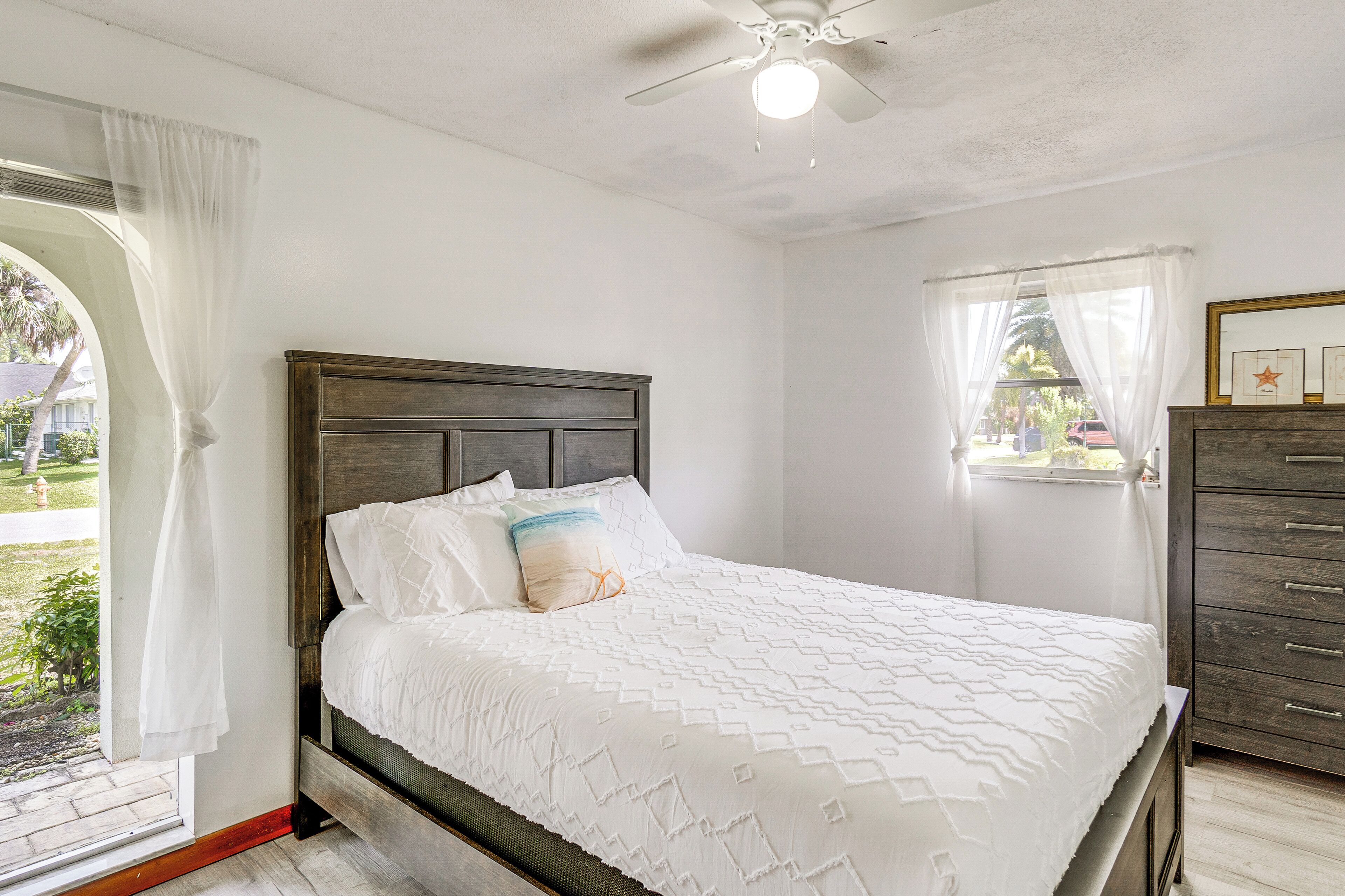 Quarto com cama, ventilador de teto, janela com cortinas e cômoda.