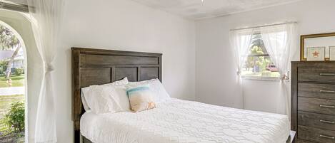 Quarto com cama, ventilador de teto, janela com cortinas e cômoda.