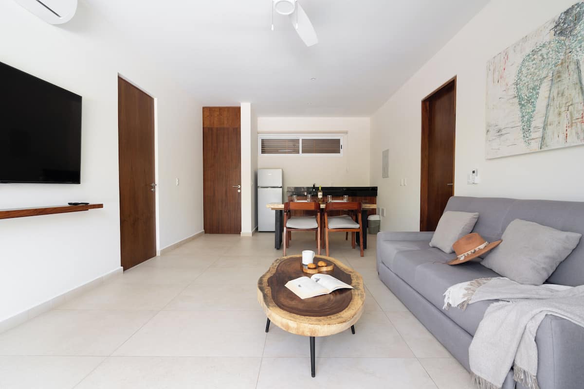 Uma sala de estar moderna com um sofá cinzento, uma mesa de centro de madeira e uma televisão de tela plana fixada na parede.