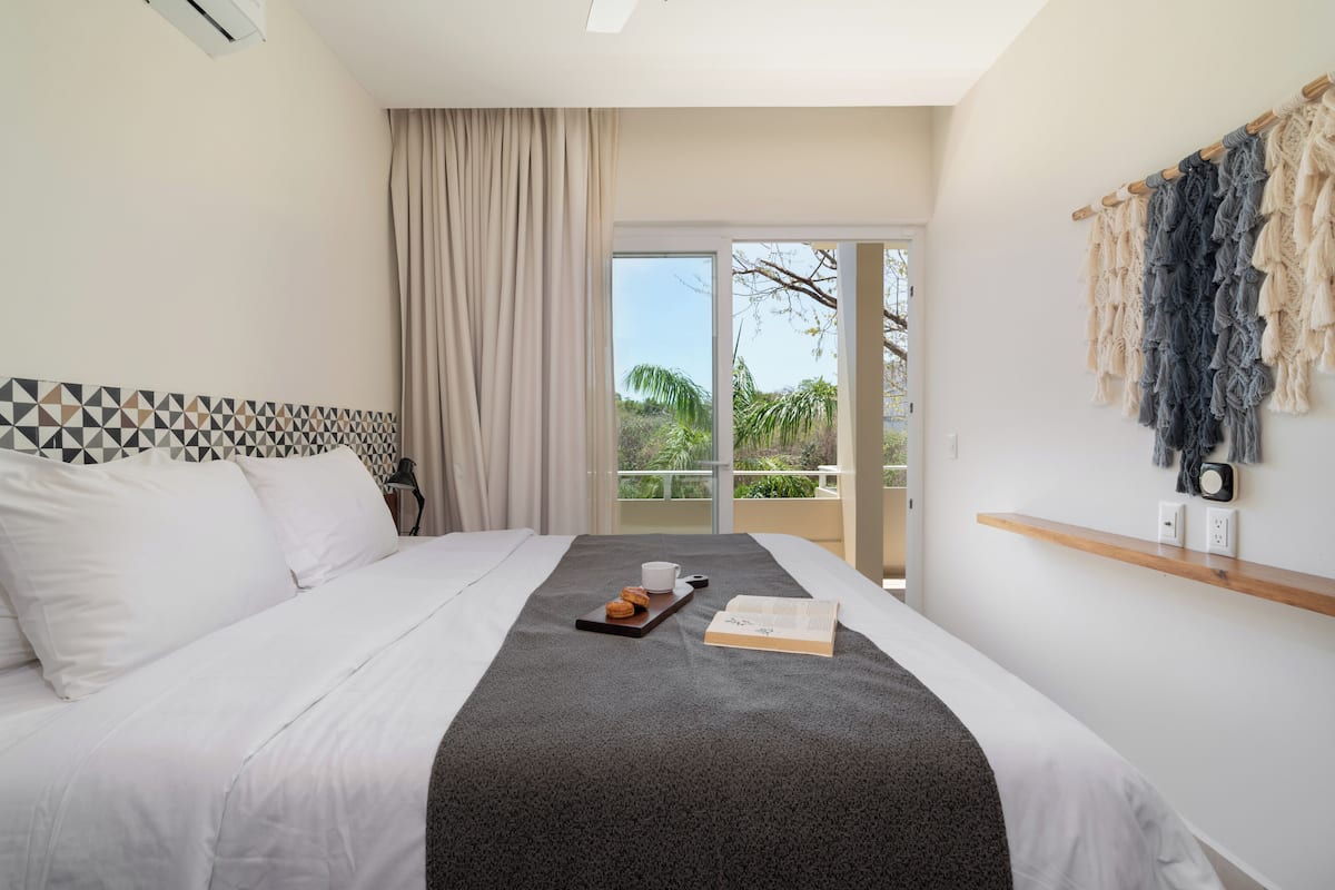 Quarto de hotel com uma cama, um tabuleiro com doces, uma chávena e um livro.