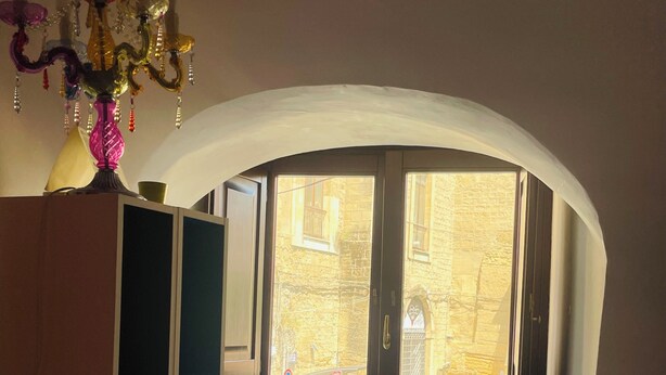 Um quarto com uma grande porta arqueada que dá para uma área externa, uma estante de livros e um candelabro.
