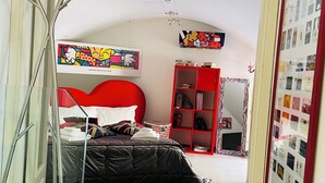 Quarto com cama, estante vermelha e parede decorada com obras de arte.