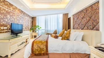 Quarto de hotel com uma cama grande, televisão, uma planta e uma cabeceira decorativa.