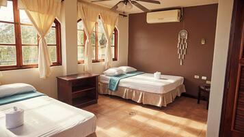 Quarto com duas camas, ventilador de teto, aparelho de ar condicionado e um apanhador de sonhos na parede.