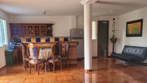 Uma sala de estar ampla com uma mesa de jantar e cadeiras, um sofá, uma cozinha com armários de madeira e piso ladrilhado.