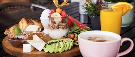 Disposição de café da manhã com croissants, iogurte, frutas e um copo de suco de laranja sobre uma mesa de madeira.
