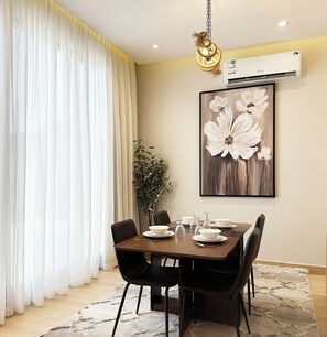 Uma área de refeições com uma mesa de madeira, cadeiras pretas, um tapete branco e uma grande pintura floral na parede.