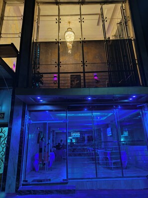 Entrada de hotel com fachada de vidro, um lustre e escadaria que leva a um andar superior.