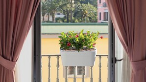 Uma varanda com planta em vaso, cortinas e vista para prédios e árvores.