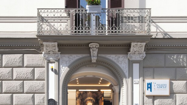 Entrada de um edifício com varanda, porta e uma placa indicando 'Palazzo Adele'.