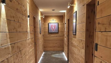 Um corredor revestido de madeira com iluminação embutida, um brasão emoldurado na parede e uma porta à direita.