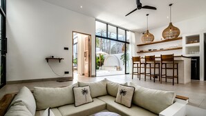 Uma sala de estar moderna com sofá seccional, mesa de centro redonda e área de jantar com cadeiras de madeira e balcão.