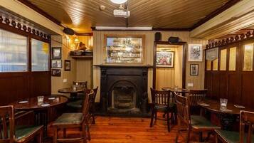 Um pub acolhedor com paredes de madeira e uma lareira, com várias mesas e cadeiras de madeira.