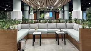 Uma área de estar moderna com um sofá curvo, duas mesinhas e diversos vasos de plantas.