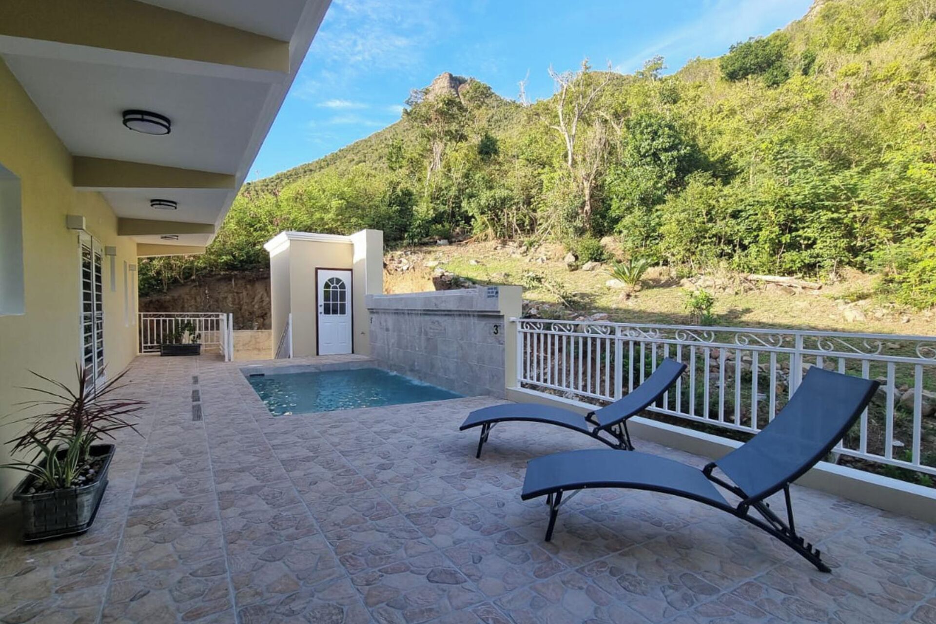 Uma área de piscina com duas espreguiçadeiras, uma porta e chão de azulejos de pedra.