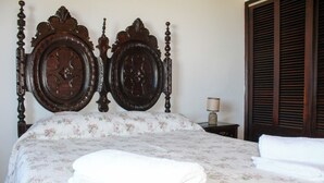 Uma cama com colcha florida, cabeceira de madeira com esculturas detalhadas e uma toalha branca sobre a cama.