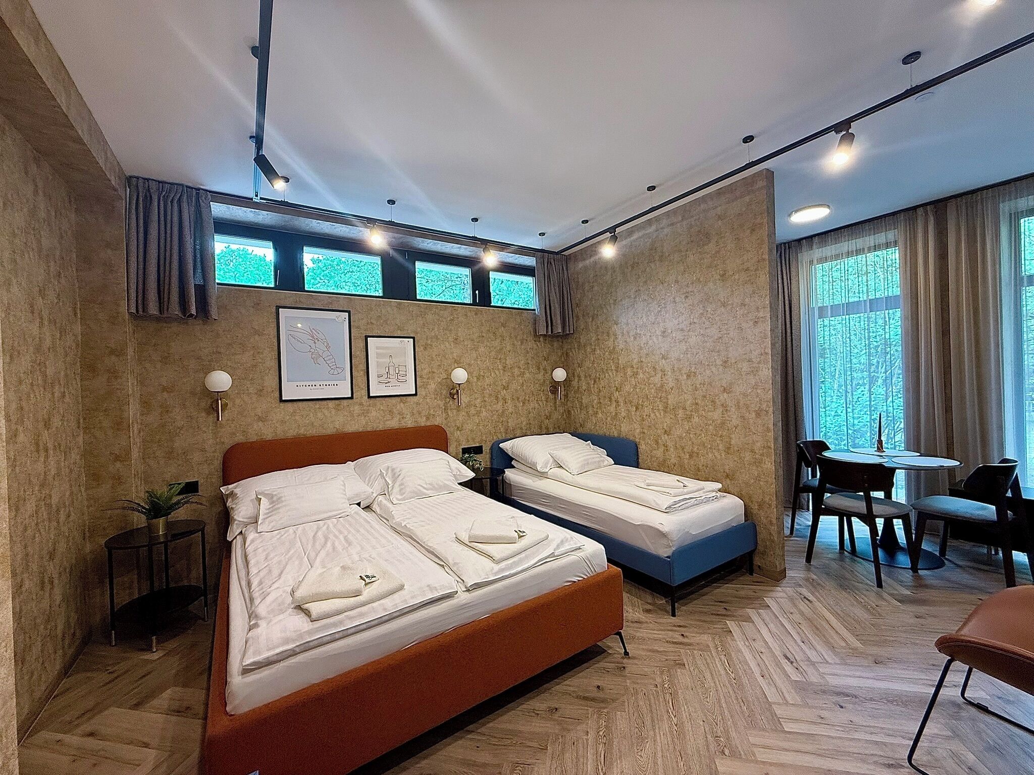 Quarto de hotel com duas camas, área de refeições e uma janela grande com cortinas.