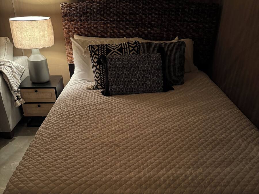 Uma cama bem arrumada com cobertura acolchoada, abajur e cabeceira de vime.