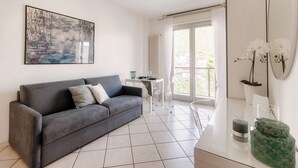 Uma sala de estar moderna com um sofá cinzento, uma mesa de jantar e uma janela grande.