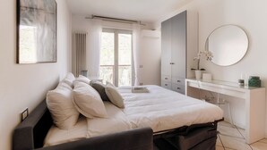Quarto com cama, mesa de cabeceira, cômoda, espelho e janela.