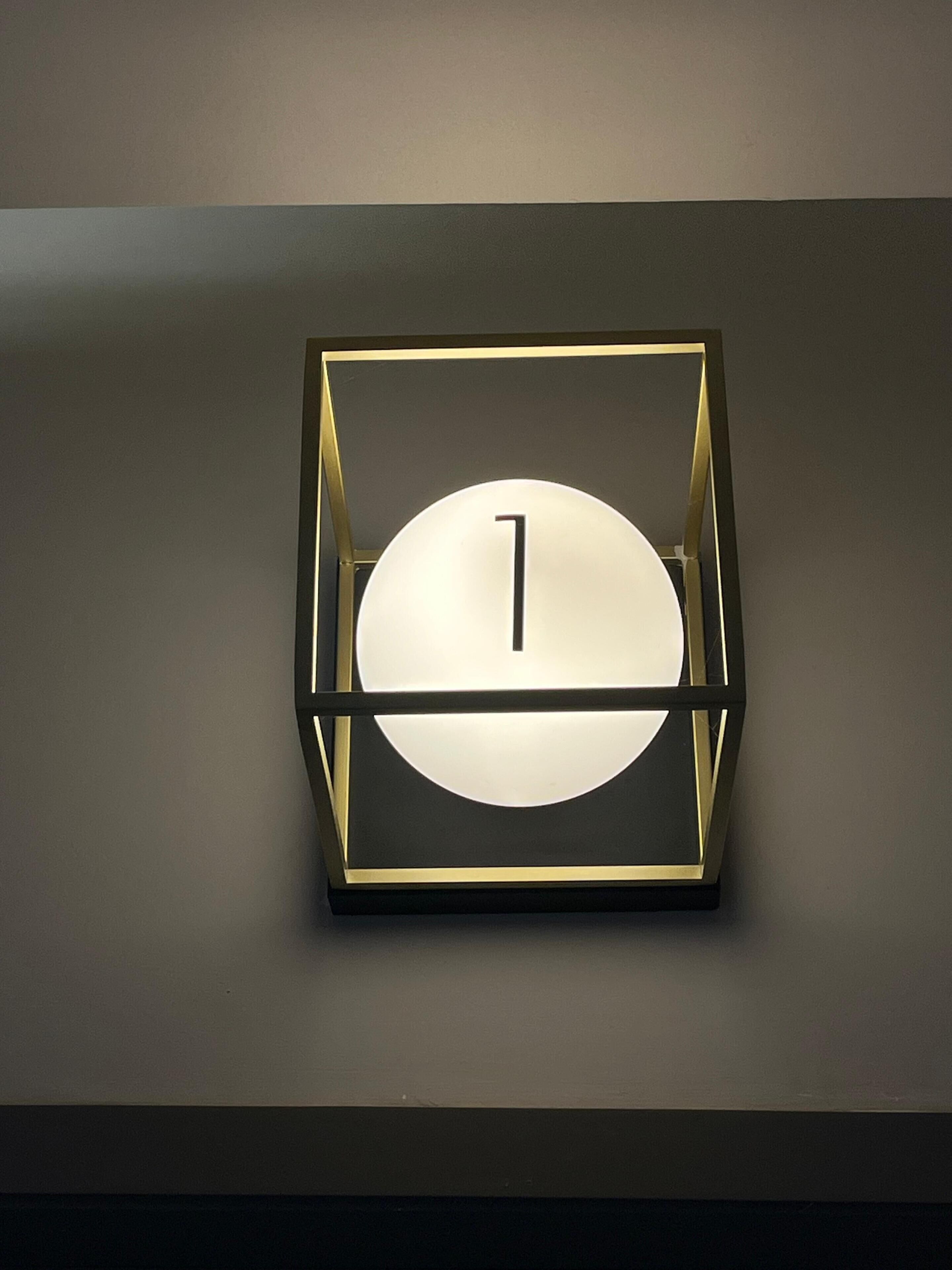 Luminária de parede com o número '1' dentro de uma moldura geométrica.