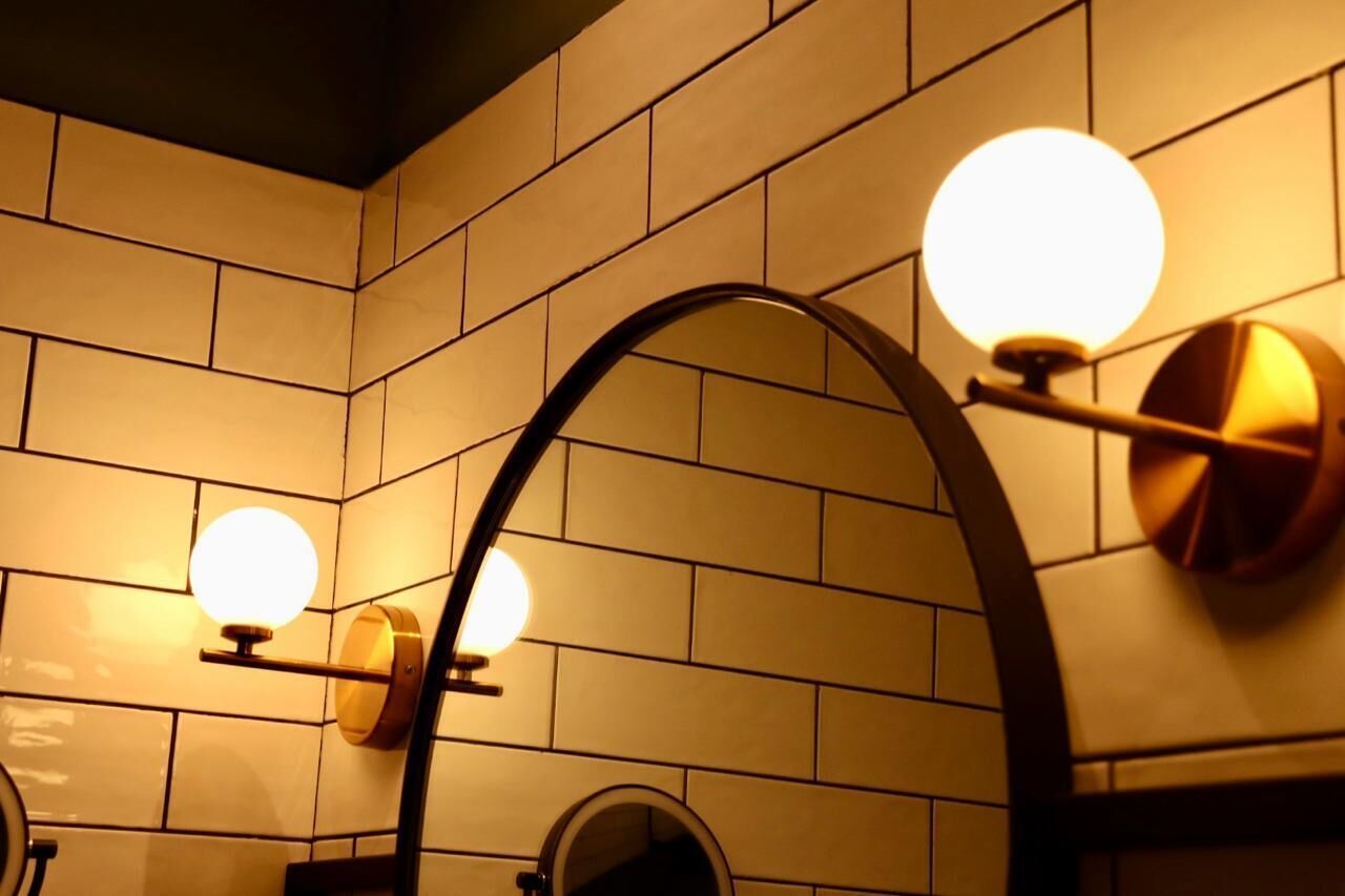 Um banheiro com paredes azulejadas, um espelho curvo e luminárias esféricas fixadas na parede.