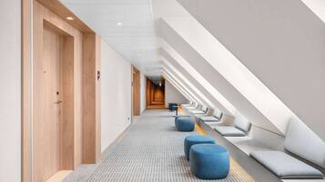 Corredor moderno de hotel com portas de madeira, teto inclinado e áreas de estar com almofadas.