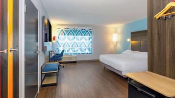 Quarto de hotel com cama, escrivaninha, cadeira, televisão e parede estampada.