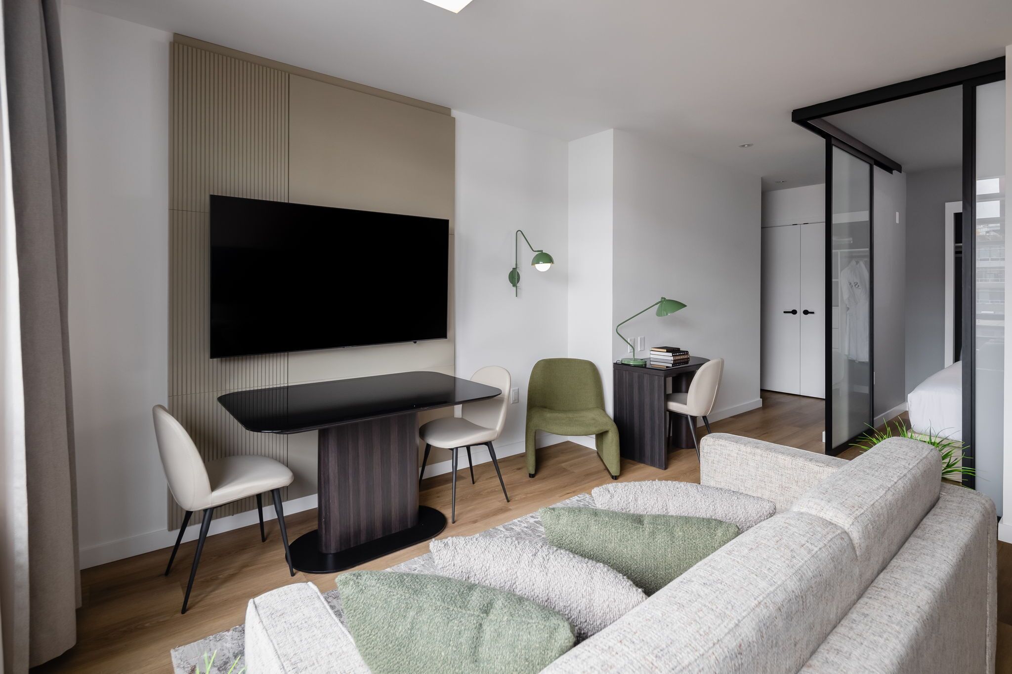 Uma sala de estar moderna com uma TV de tela plana, uma mesa de jantar, duas cadeiras, um sofá e uma pequena mesa lateral com um abajur.