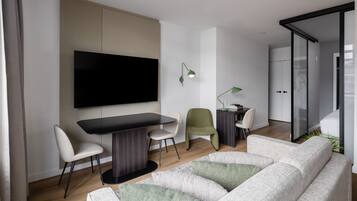 Uma sala de estar moderna com uma TV de tela plana, uma mesa de jantar, duas cadeiras, um sofá e uma pequena mesa lateral com um abajur.