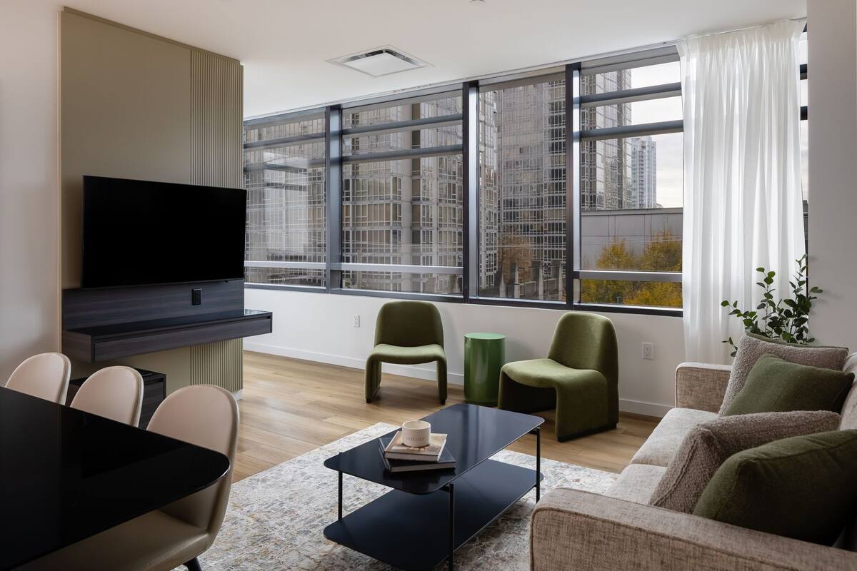 Uma sala de estar moderna com televisão de tela plana, uma mesa de jantar e duas poltronas verdes.