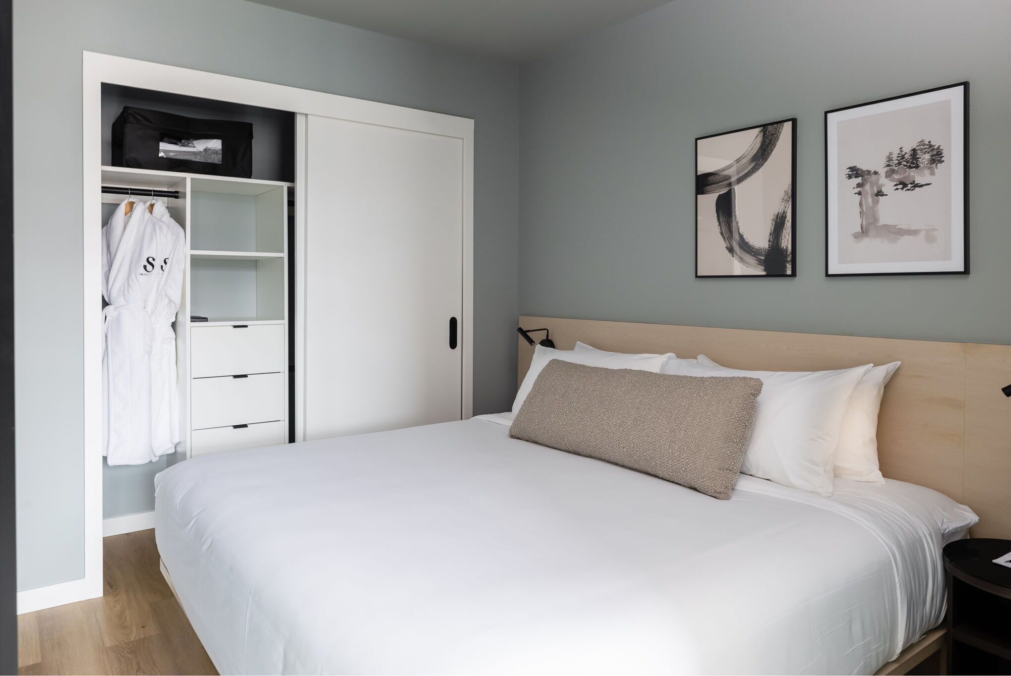 Quarto com uma cama grande, um guarda-roupa com espaço para pendurar roupas e duas obras de arte emolduradas na parede.