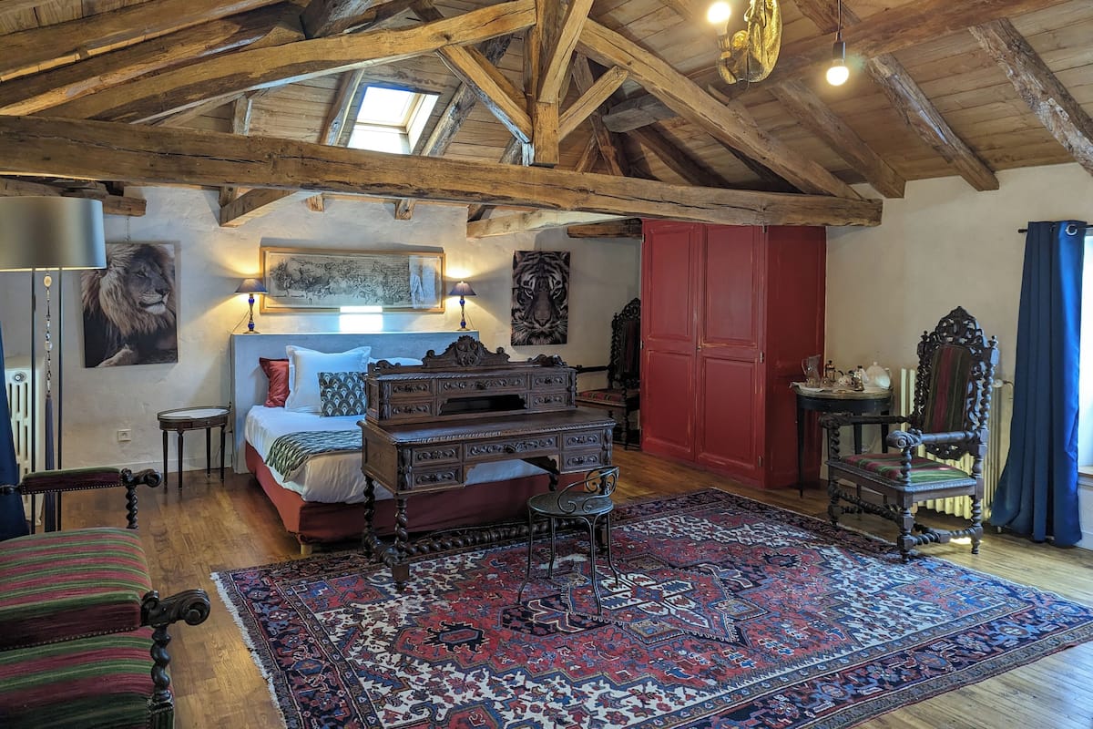 Um quarto rústico com vigas de madeira expostas, uma cama grande, um guarda-roupa vermelho e um tapete tradicional.