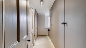 Um corredor estreito com portas fechadas em ambos os lados, um aparelho de luz no teto e uma janela no final.