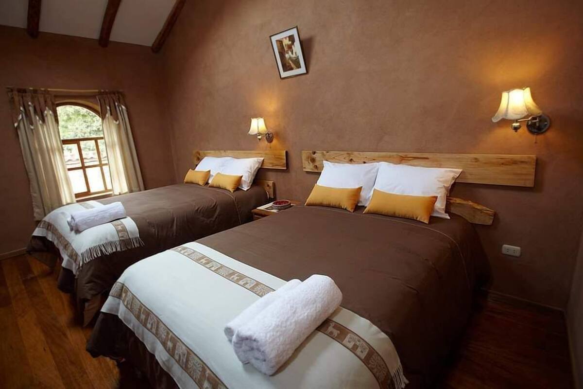 Quarto de hotel com duas camas, cabeceiras de madeira e luminárias fixadas na parede.
